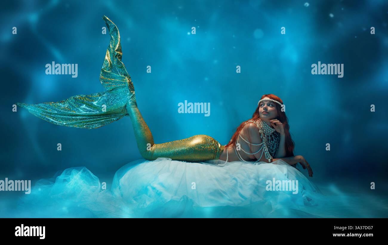 Mystical mermaid lying on sheer floating fabric, her golden tail ...