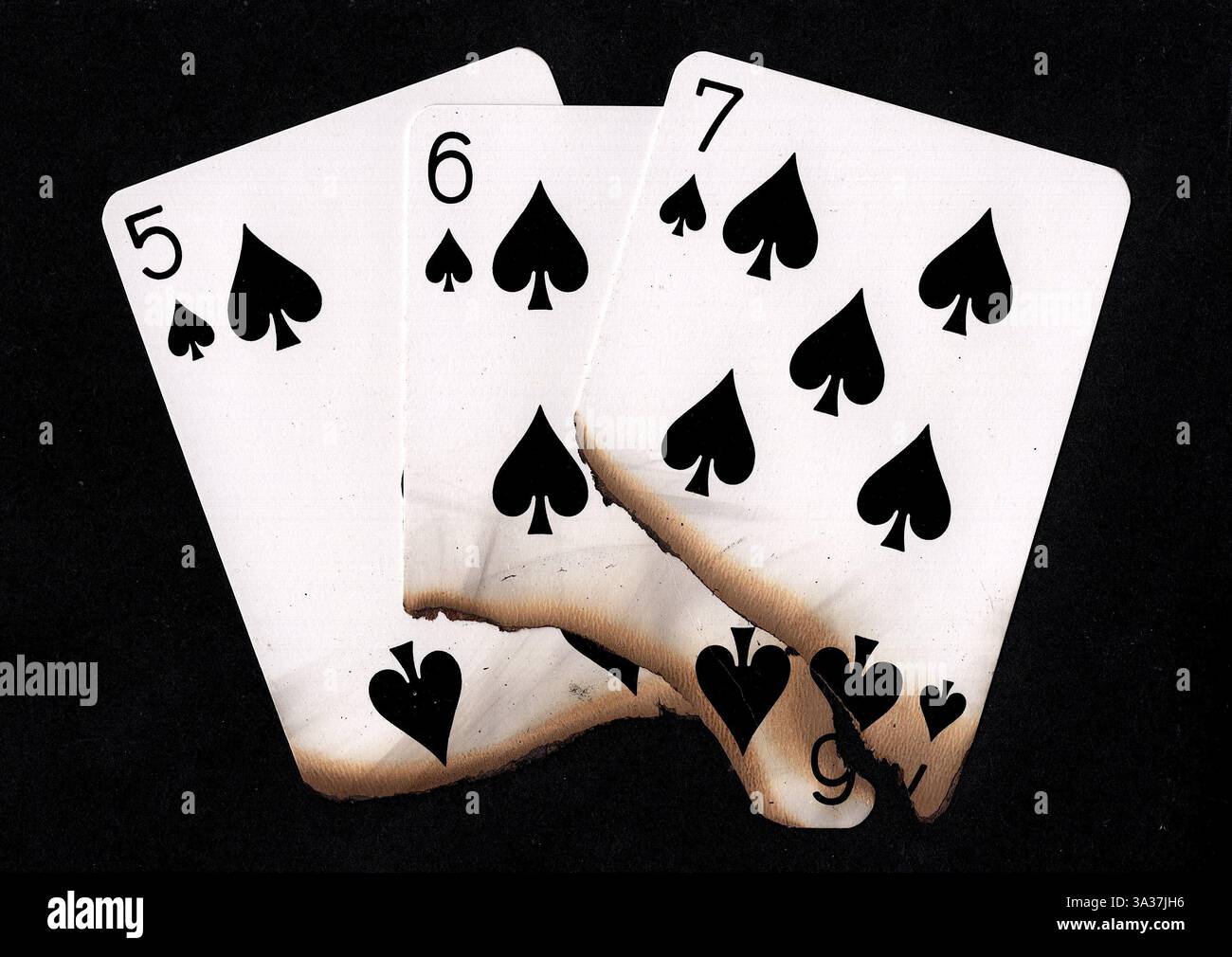 Partly burnt playing cards in the suit of spades isolated on a black ...