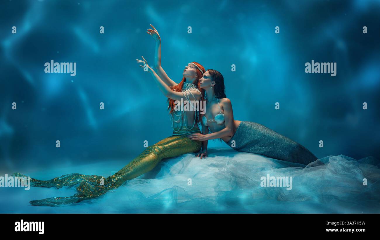 Mystical mermaid extending arms towards glowing light as another leans ...