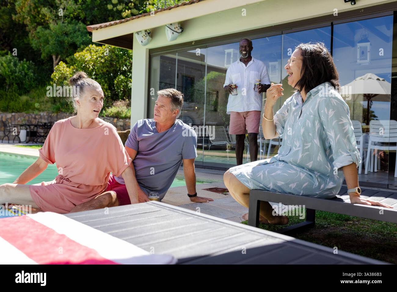 Senior friends relaxing by pool, enjoying conversation and drinks ...