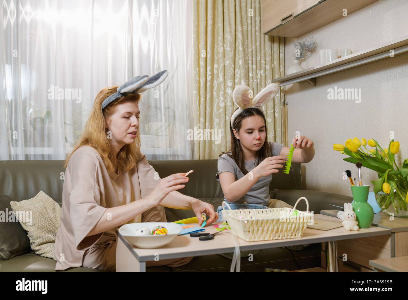 A mother and daughter wearing bunny ears are making Easter crafts in a ...
