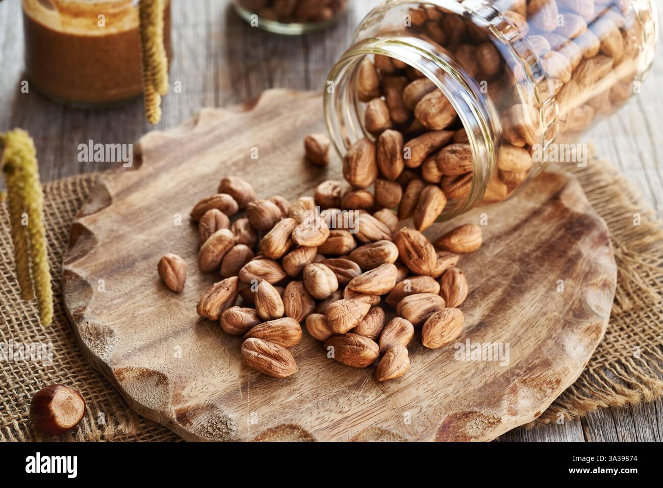 Whole hazelnuts spilled from a glass jar, with a jar of nut butter in ...