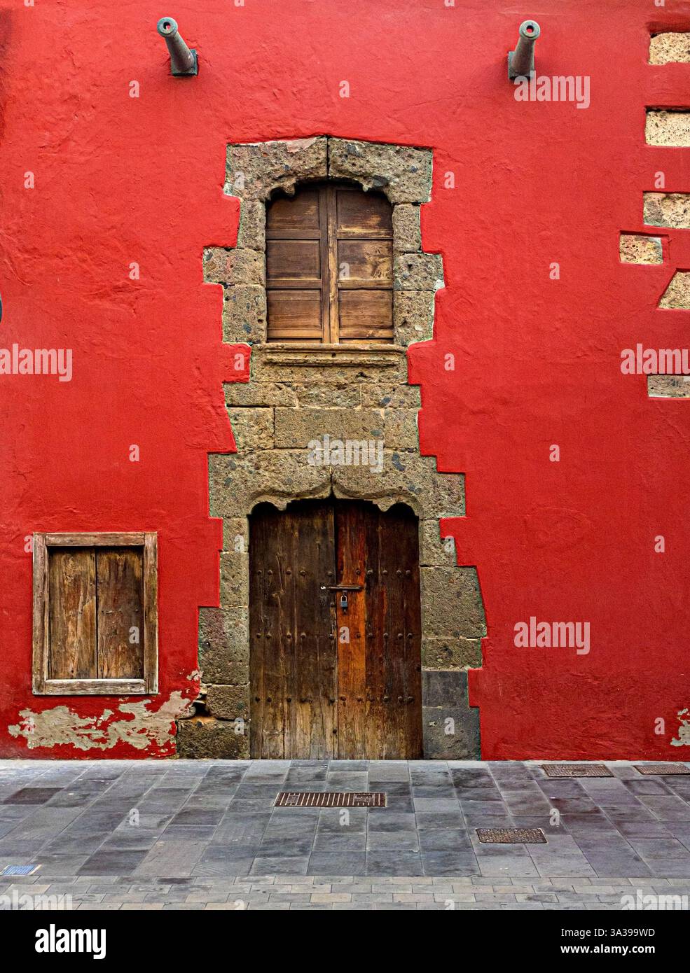 Two cannons flank a vibrant red building featuring rustic wooden doors ...