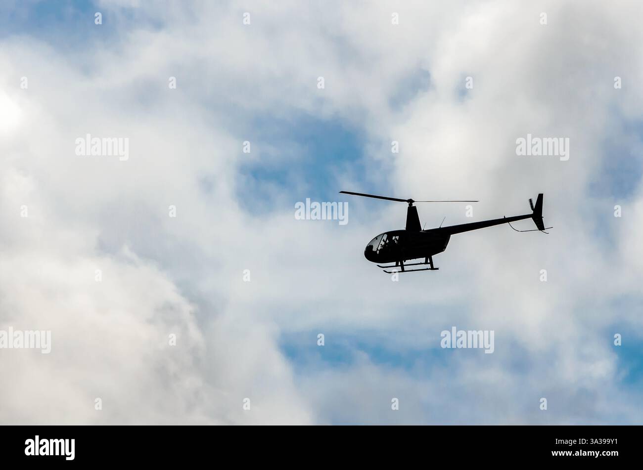 Silhouetted side view of a small private helicopter flying to the left ...