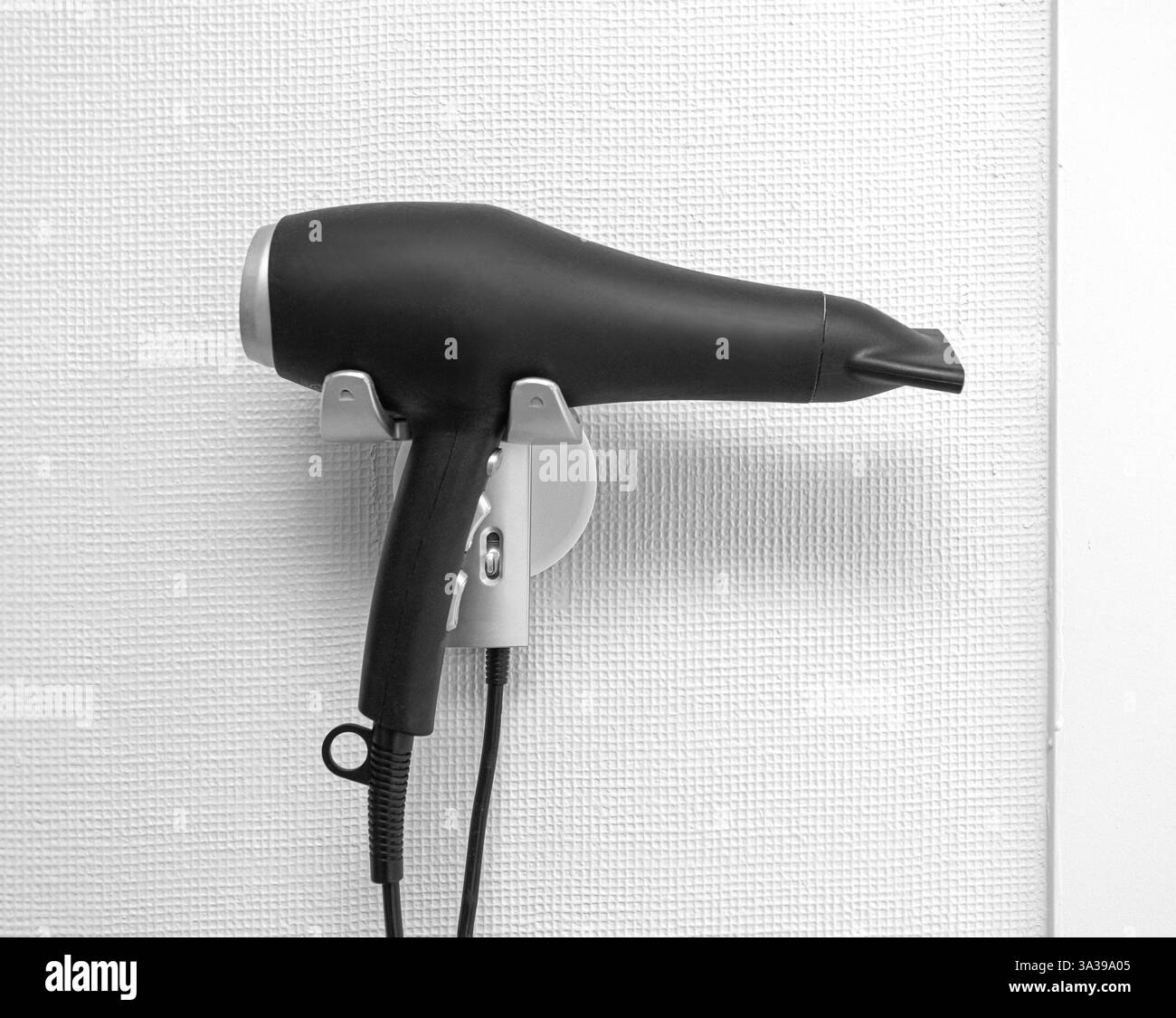 Black hair dryer hanging on wall mount in bathroom or hotel room, ready ...