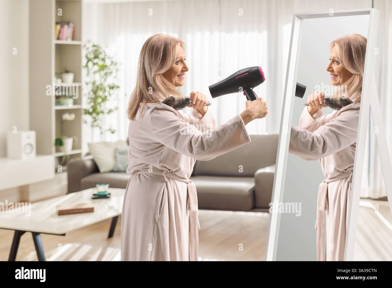 Woman blow drying hair in front of a mirror at home Stock Photo - Alamy