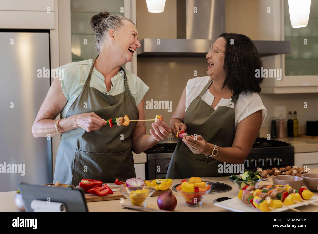 Senior women in kitchen preparing skewers and laughing together ...