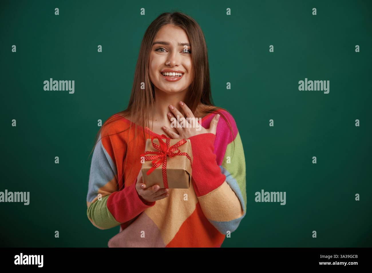 Thankful, holding little gift box. Young woman is standing against green background in the ...