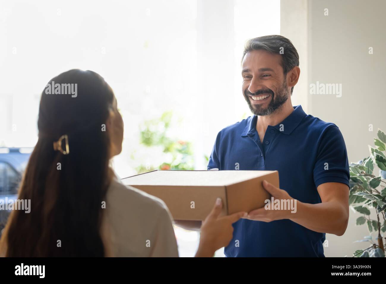 Happy courier man giving logistic cardboard box to female customer ...