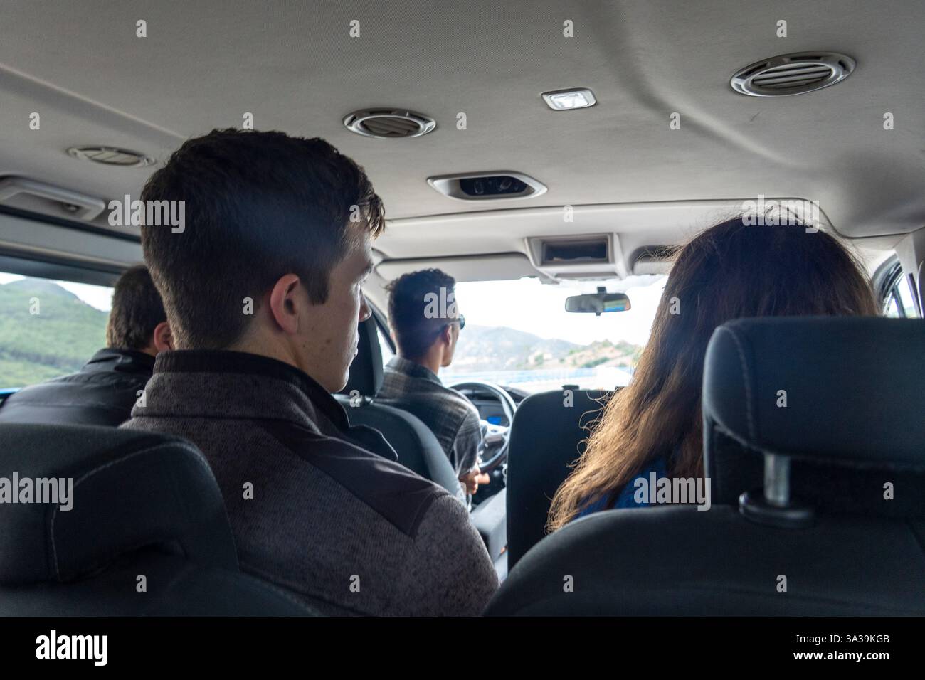 A group of several people can be seen sitting in the back seat of a van ...
