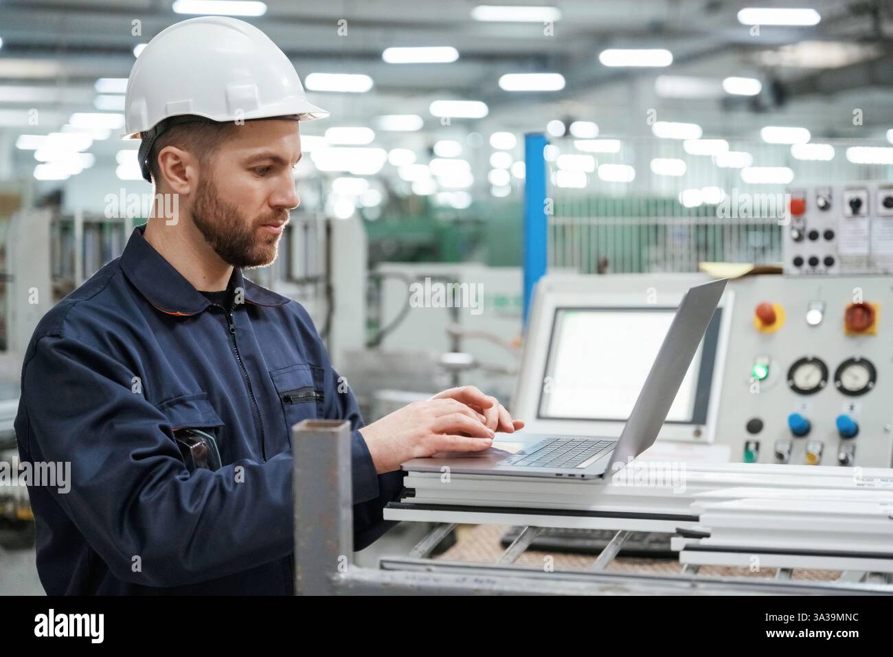 Using the laptop. Factory worker is indoors with hard hat Stock Photo ...