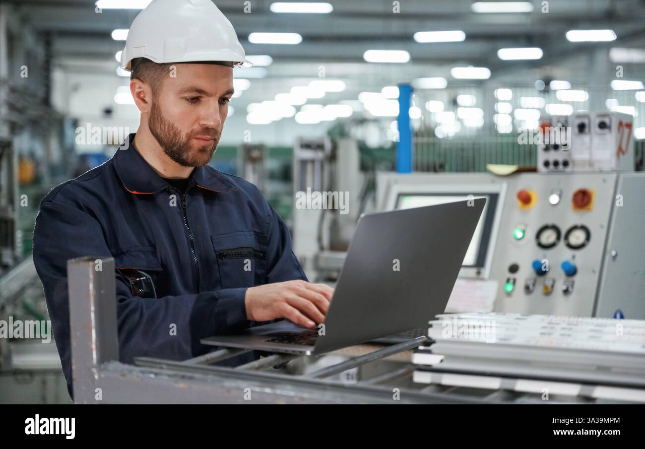 Using the laptop. Factory worker is indoors with hard hat Stock Photo ...