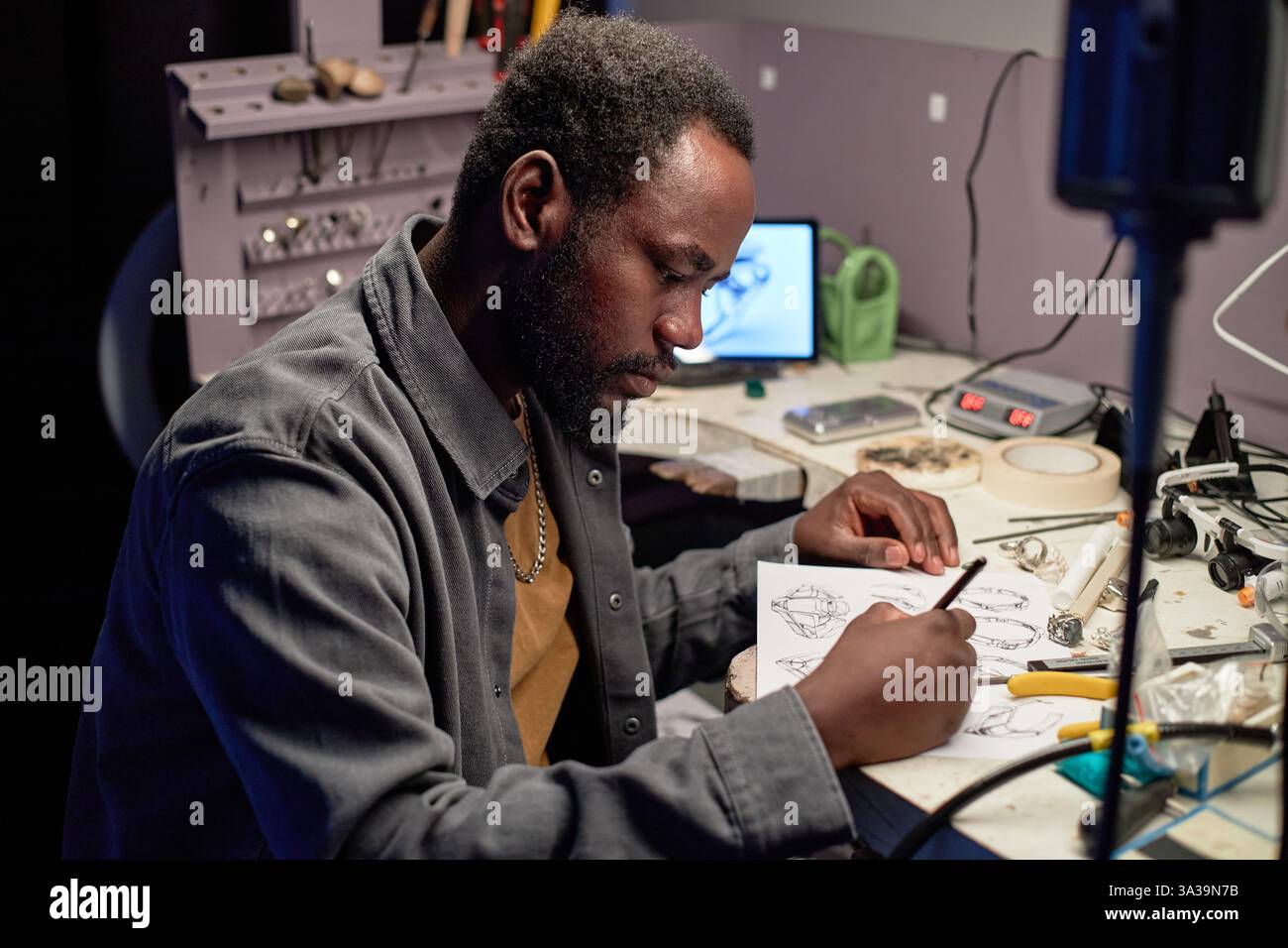 Focused man working on technical drawing in workshop environment with ...