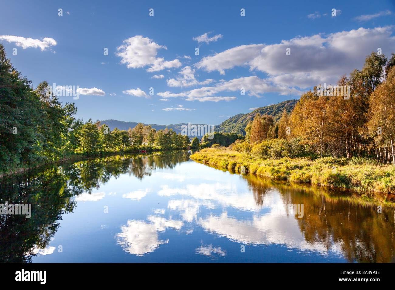 Calm river water in center of Lyngdal mirrors the clear blue sky and ...