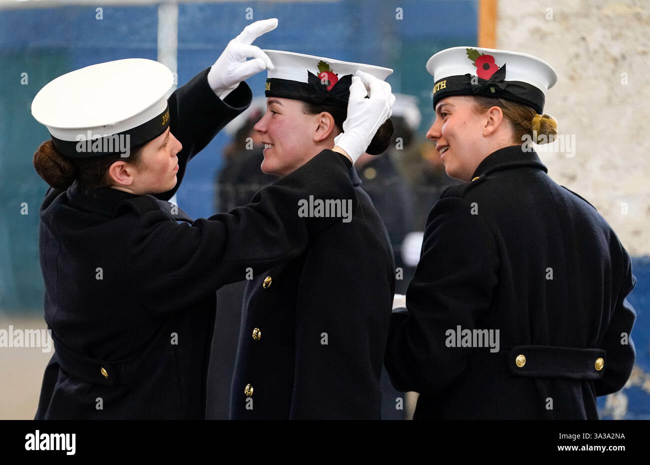 A Royal Navy rating has their poppy adjusted on their cap by a ...