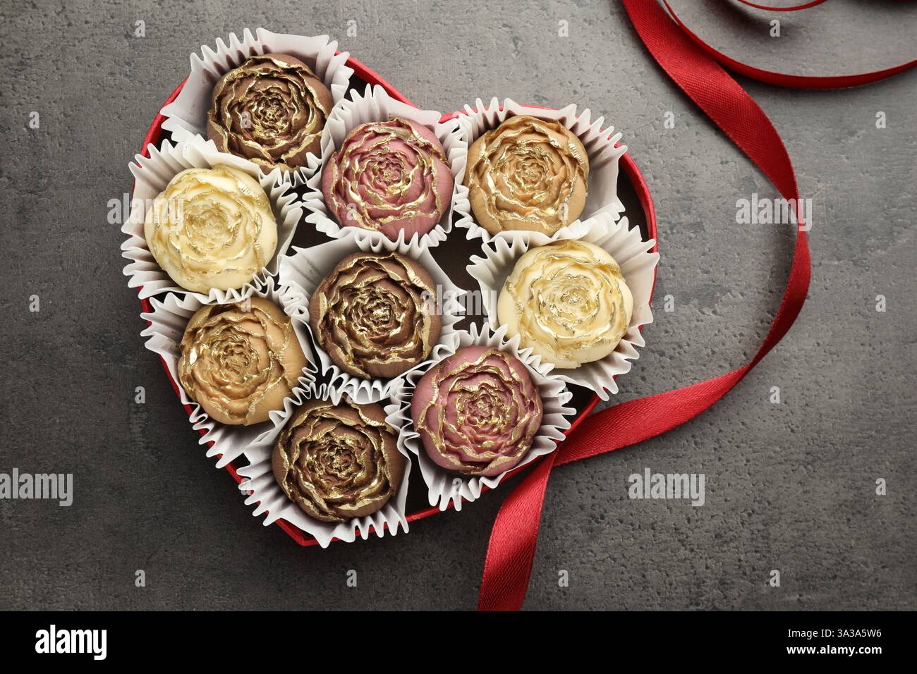 Flower shaped chocolate bonbons in box and red ribbon on grey table ...