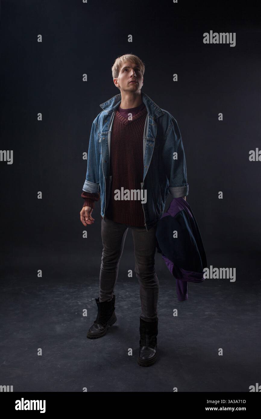 person stands confidently wearing a denim jacket over a maroon sweater ...