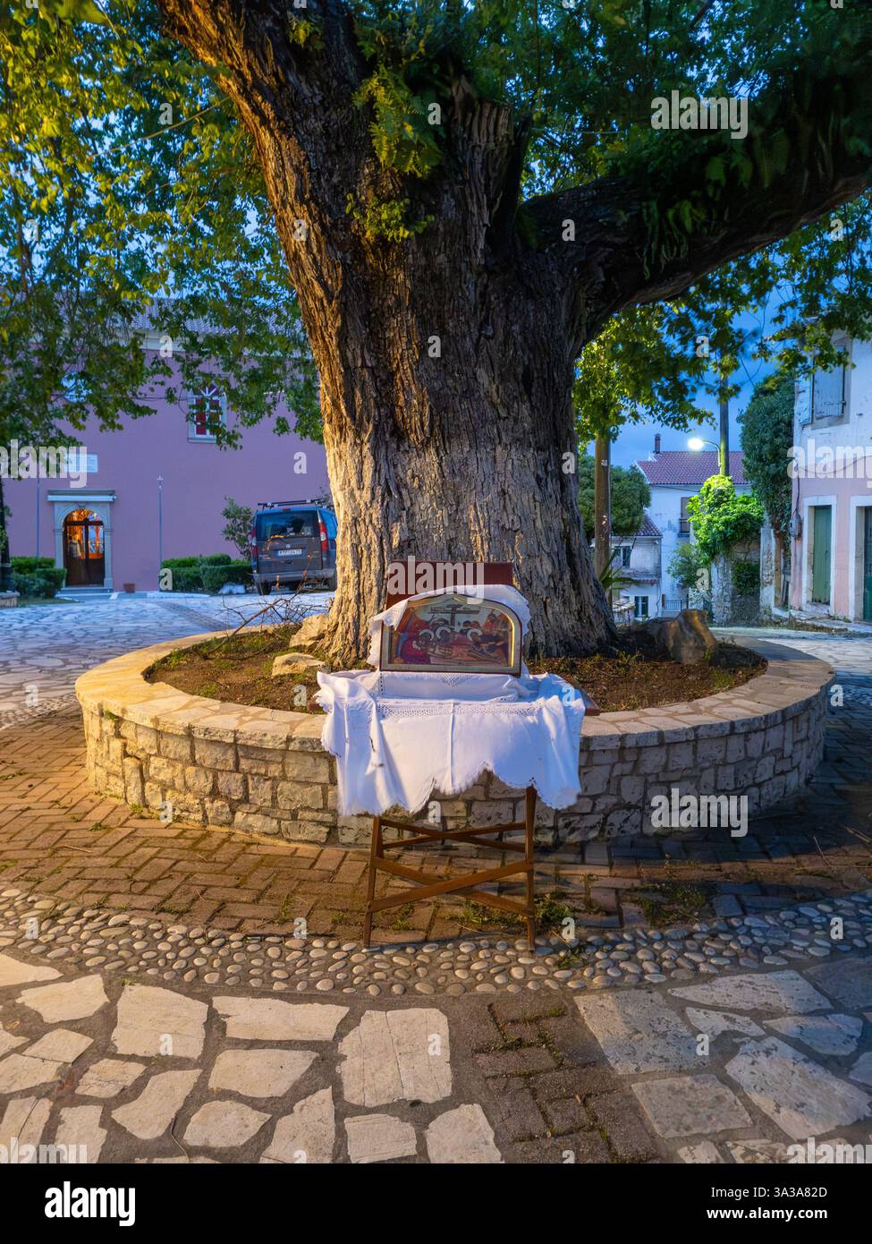 An outdoor altar stands beneath a large tree in a cobblestone village ...