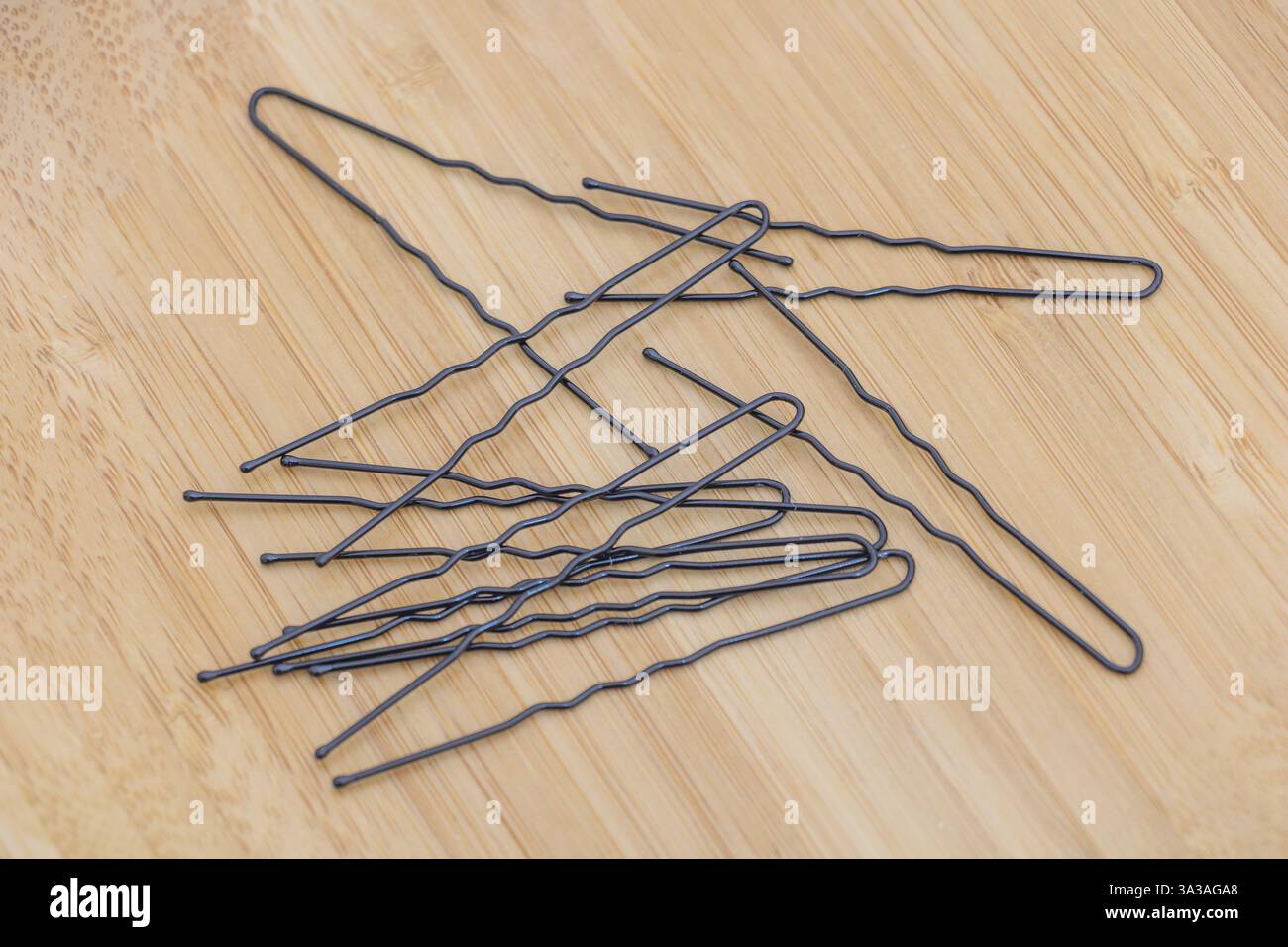 A set of hair pins, thin black metal clips on a light wooden table, top ...
