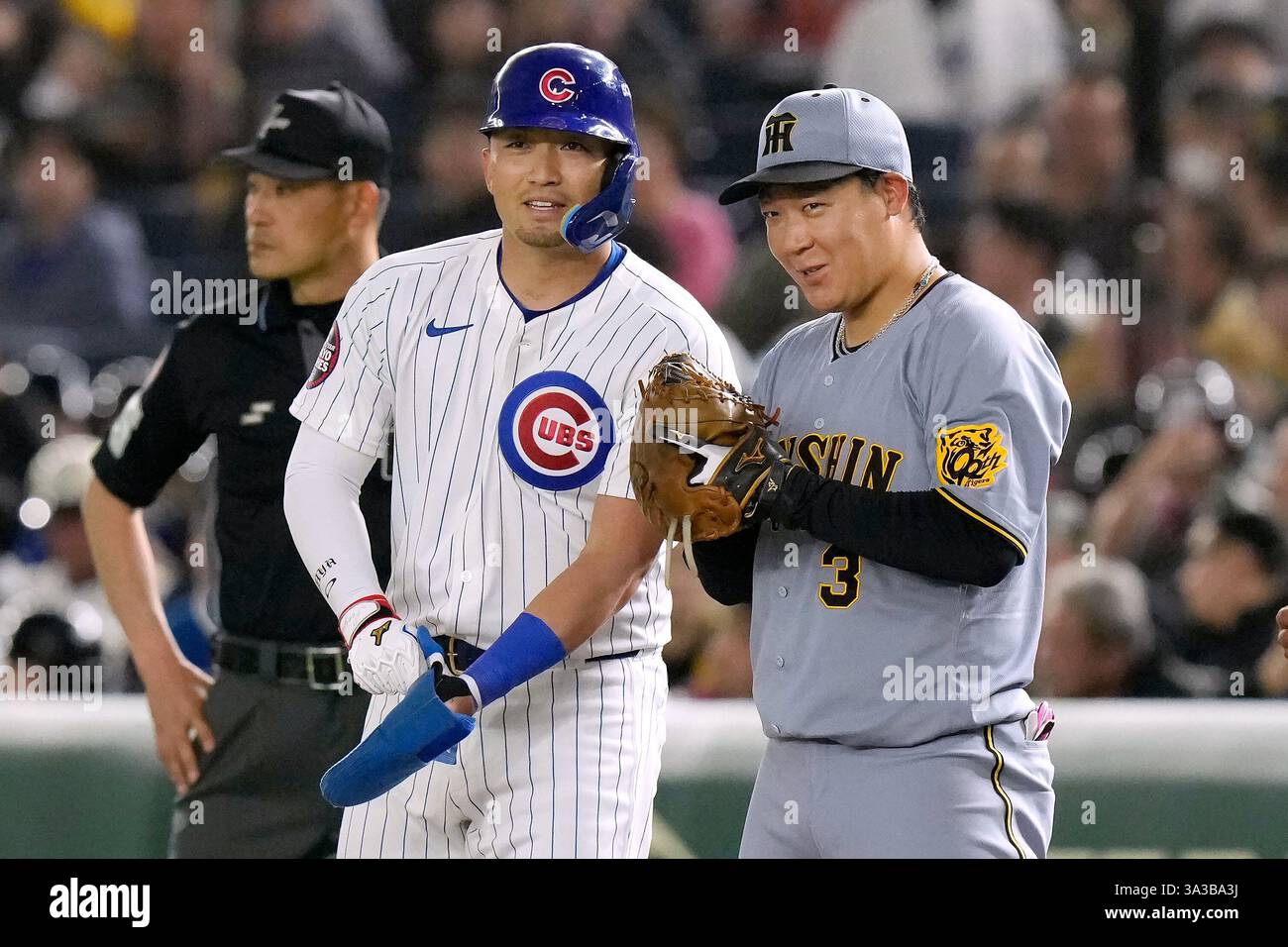Chicago Cubs' Seiya Suzuki, middle, stands at first base after hitting a single next to Hanshin ...