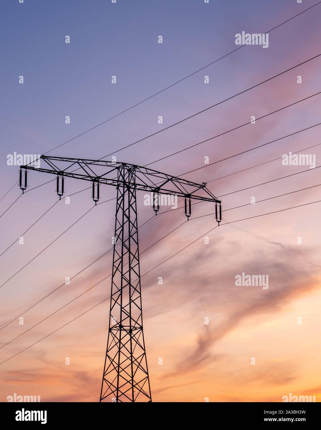 High voltage poles with strung wires stand out against beautiful sunset ...
