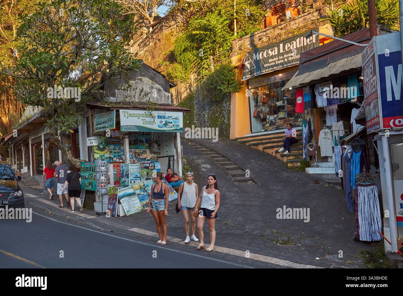 Three young women waiting to cross Jalan Raya Ubud, the maiin street in ...