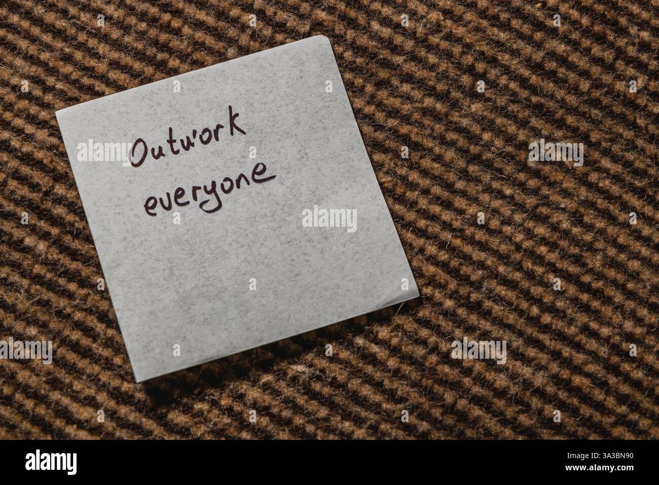 A handwritten note on a textured surface prompts everyone to outwork ...