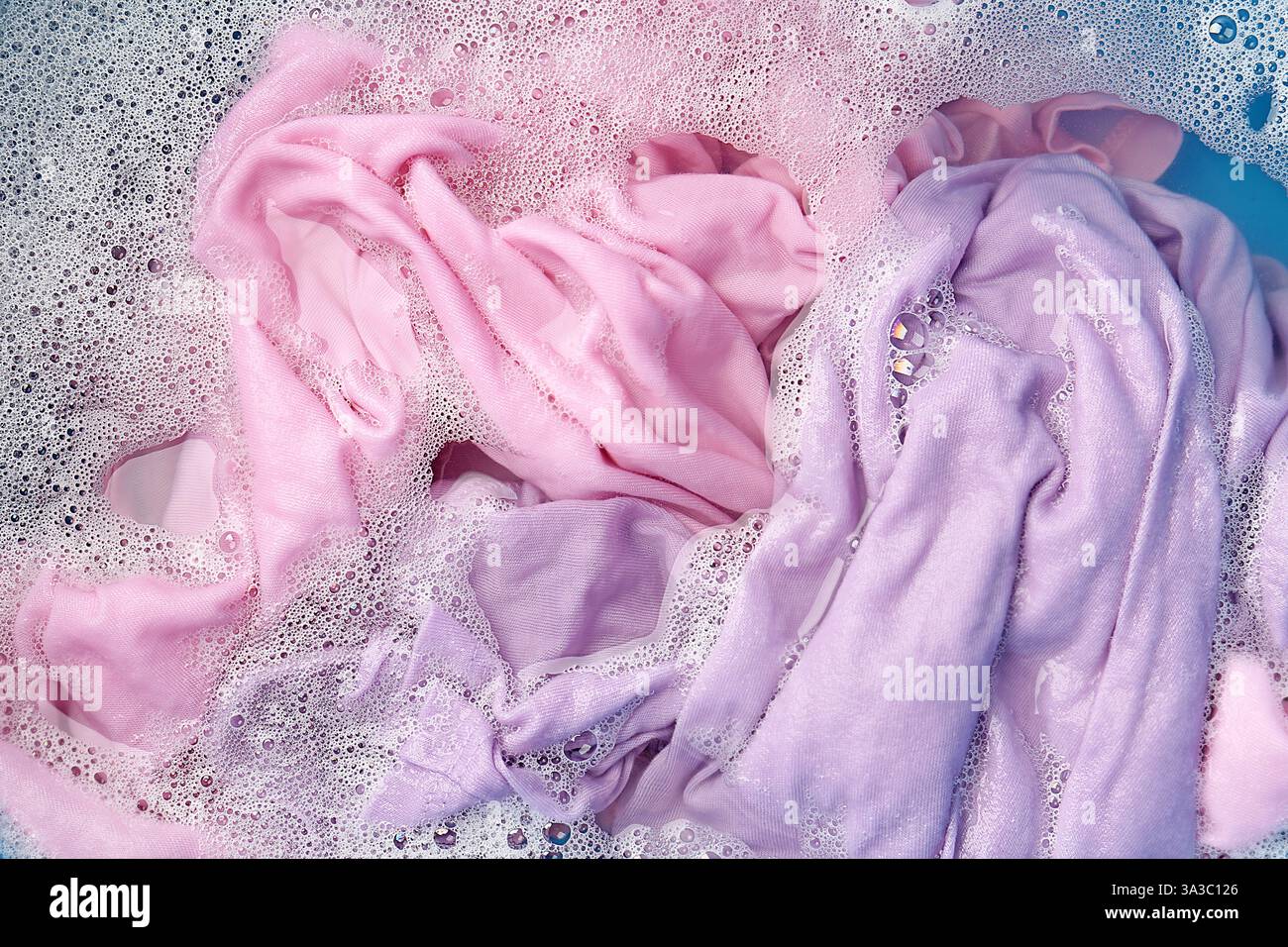 Colorful clothes soaked in water before washing, top view Stock Photo ...