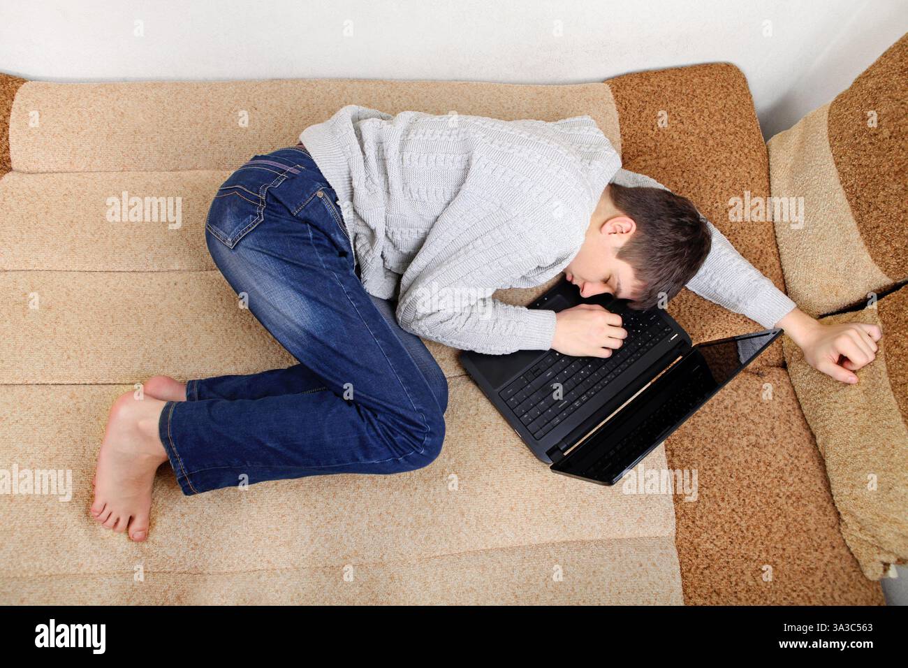 Tired Teenager falling asleep with Laptop on Sofa Stock Photo - Alamy