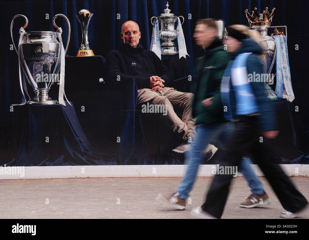 A Manchester City fan walks past a picture of manager Pep Guardiola ...