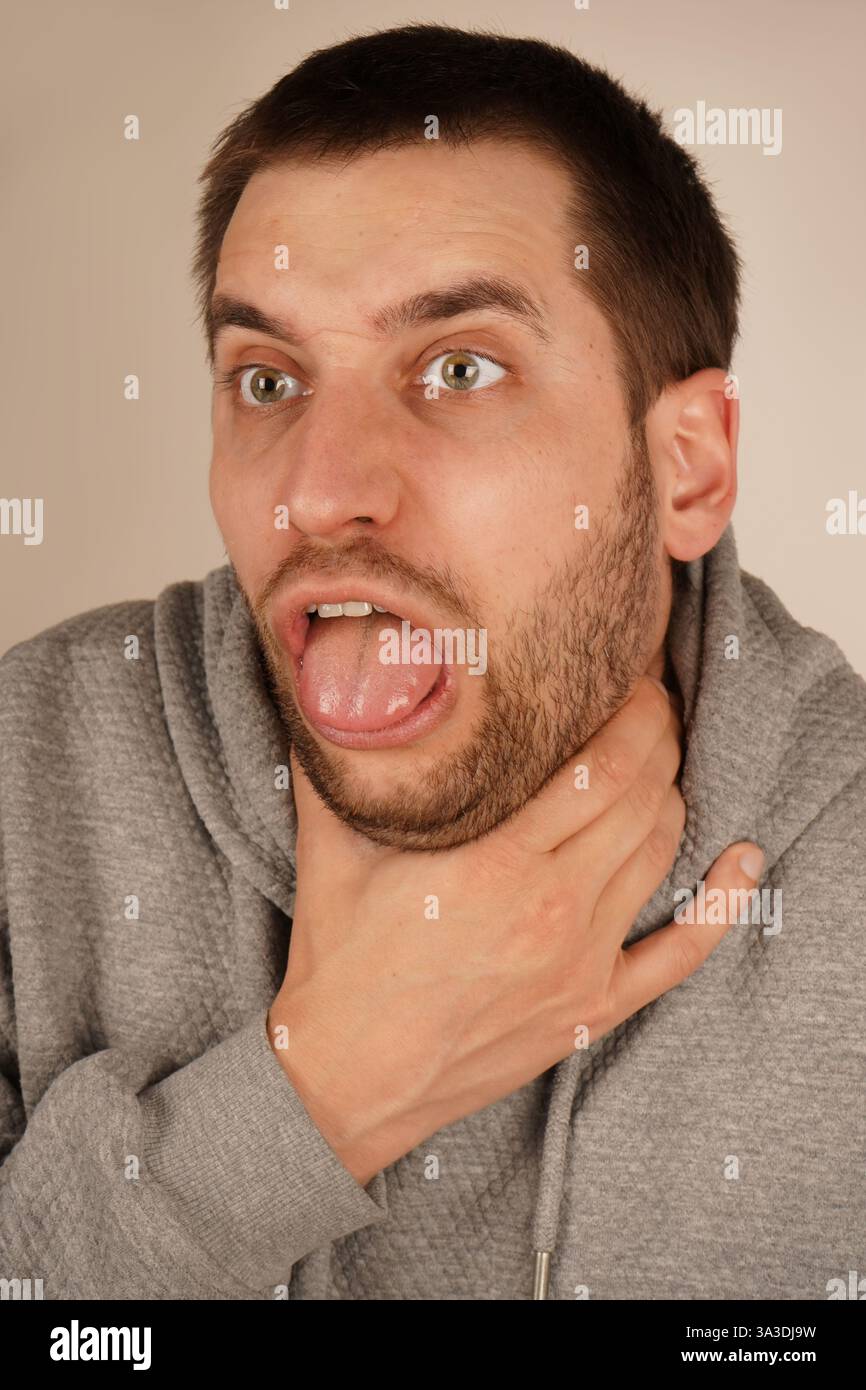 A man holds his throat with one hand, opening his mouth as if he is ...