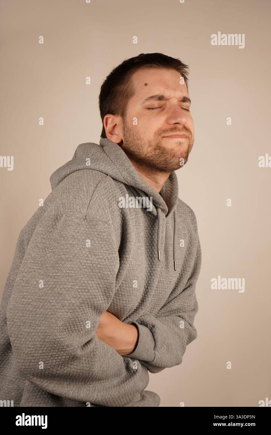 A young man is bending forward, pressing his hands against his stomach ...