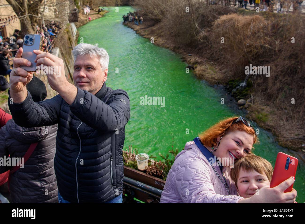 People take selfies against the green-tinted waters of the Vilia River ...