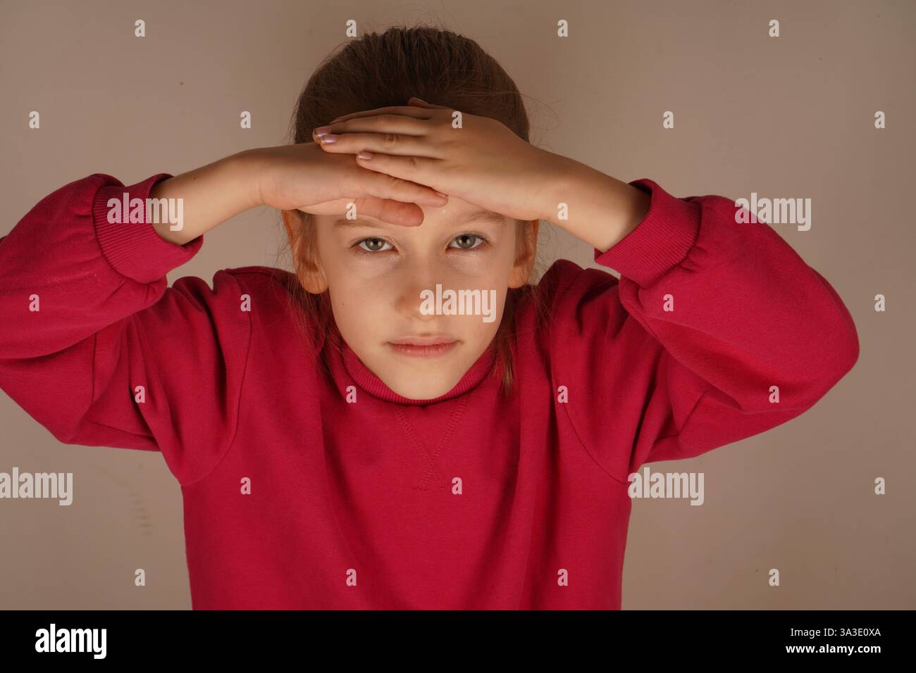 Shading her eyes with one hand, the girl tries to block the strong ...