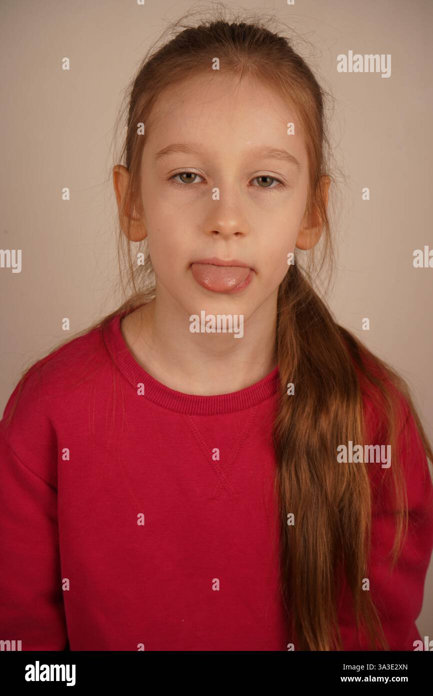 A playful girl sticks out her tongue with a cheerful expression. Her casual pose reflects ...