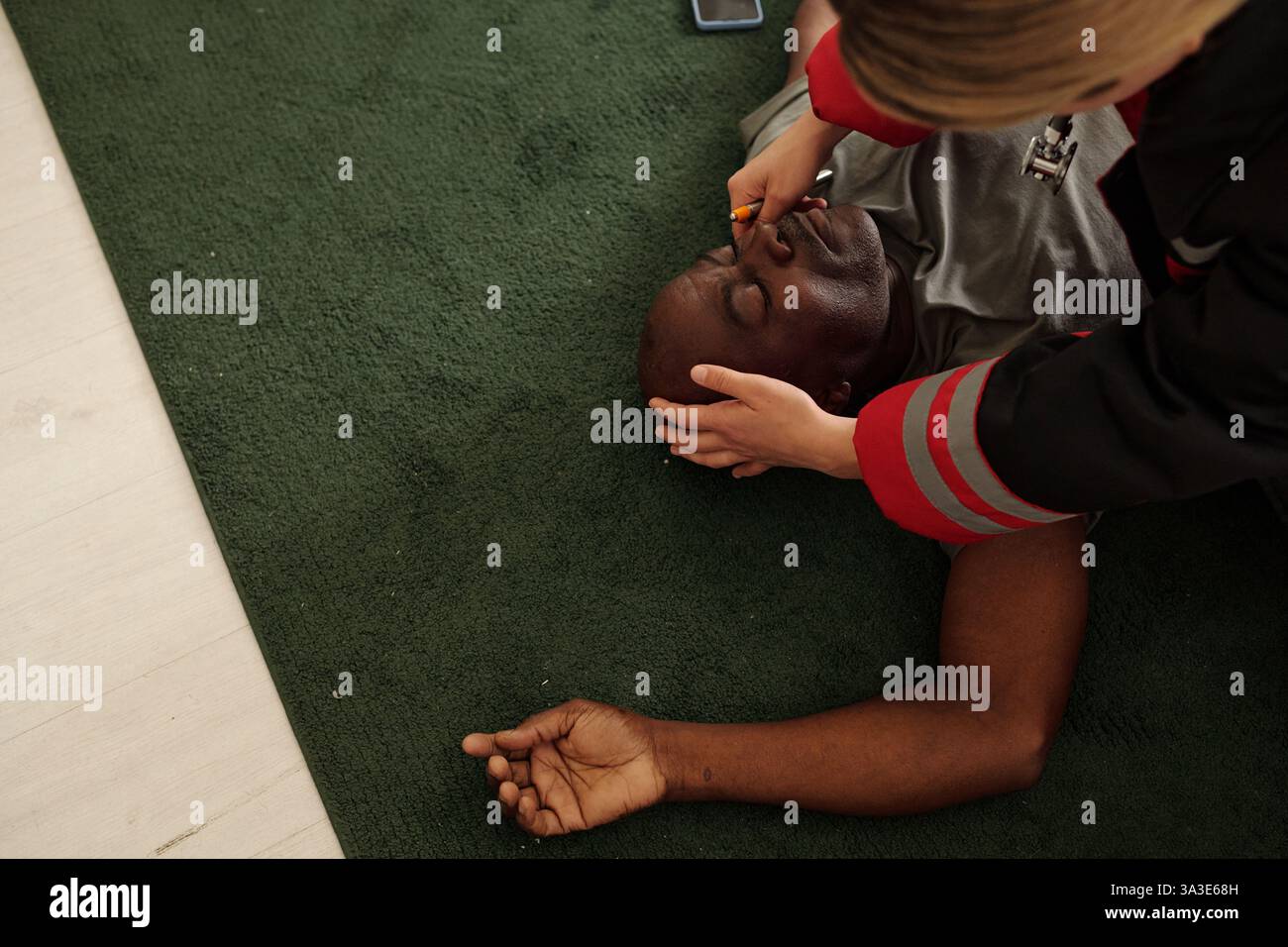 Paramedic attending to unconscious man lying on floor, providing medical assistance, checking ...