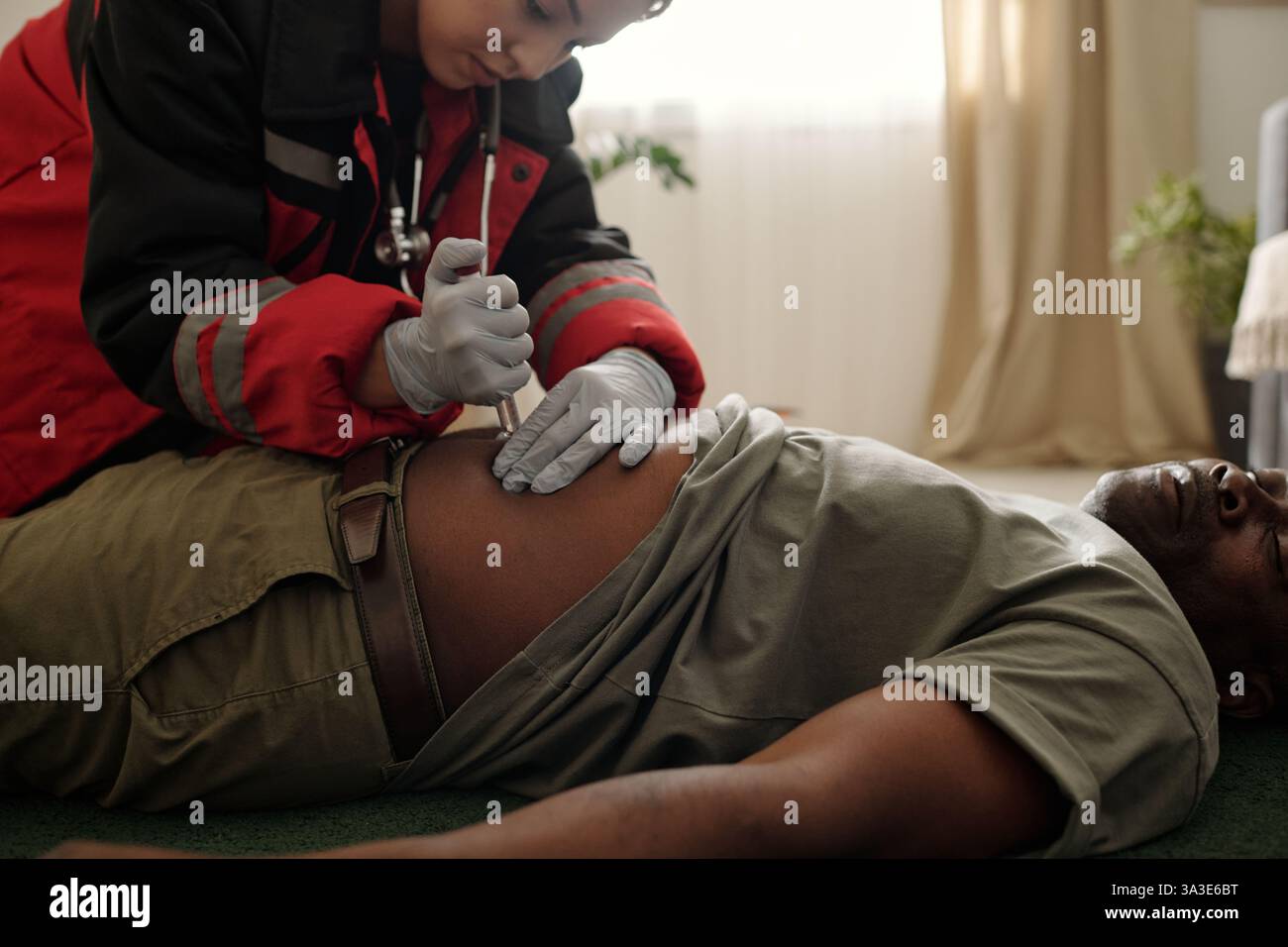 Emergency medical responder performing CPR on unconscious African American man lying on floor ...