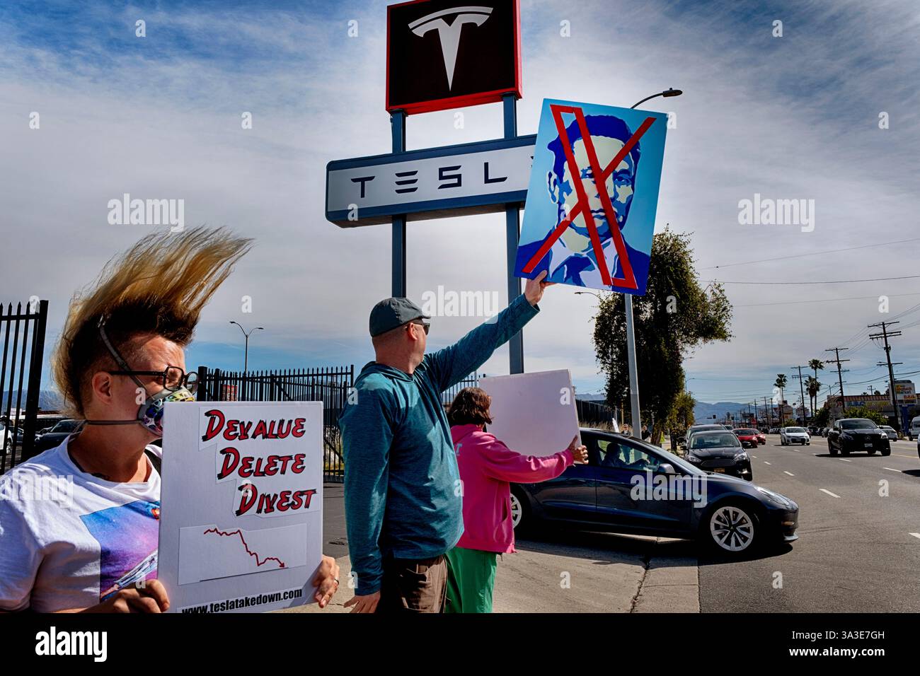 Protesters carrying signs and chanting slogans stand outside a Tesla ...