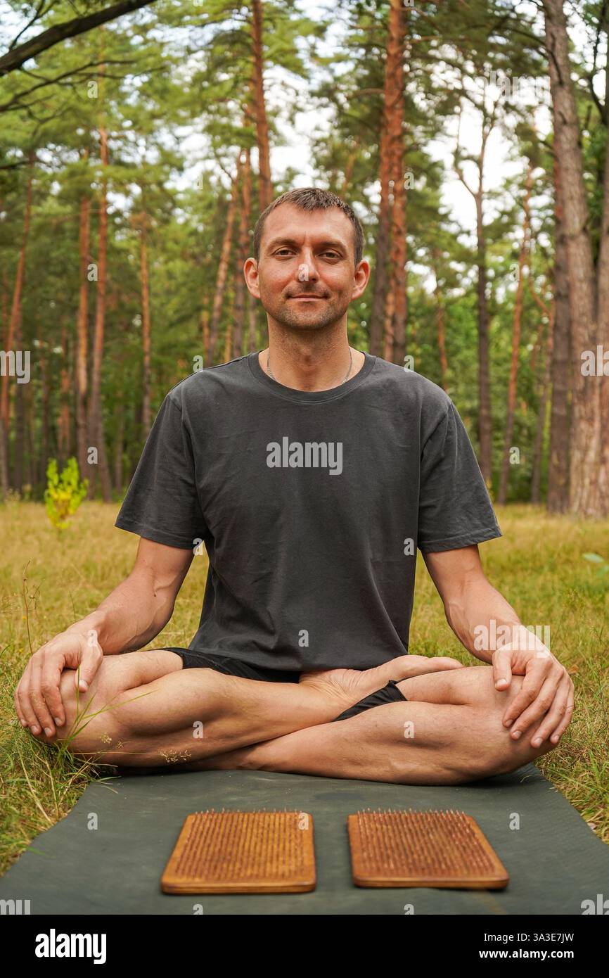 A man sits cross-legged in the lotus position on a green mat in the ...