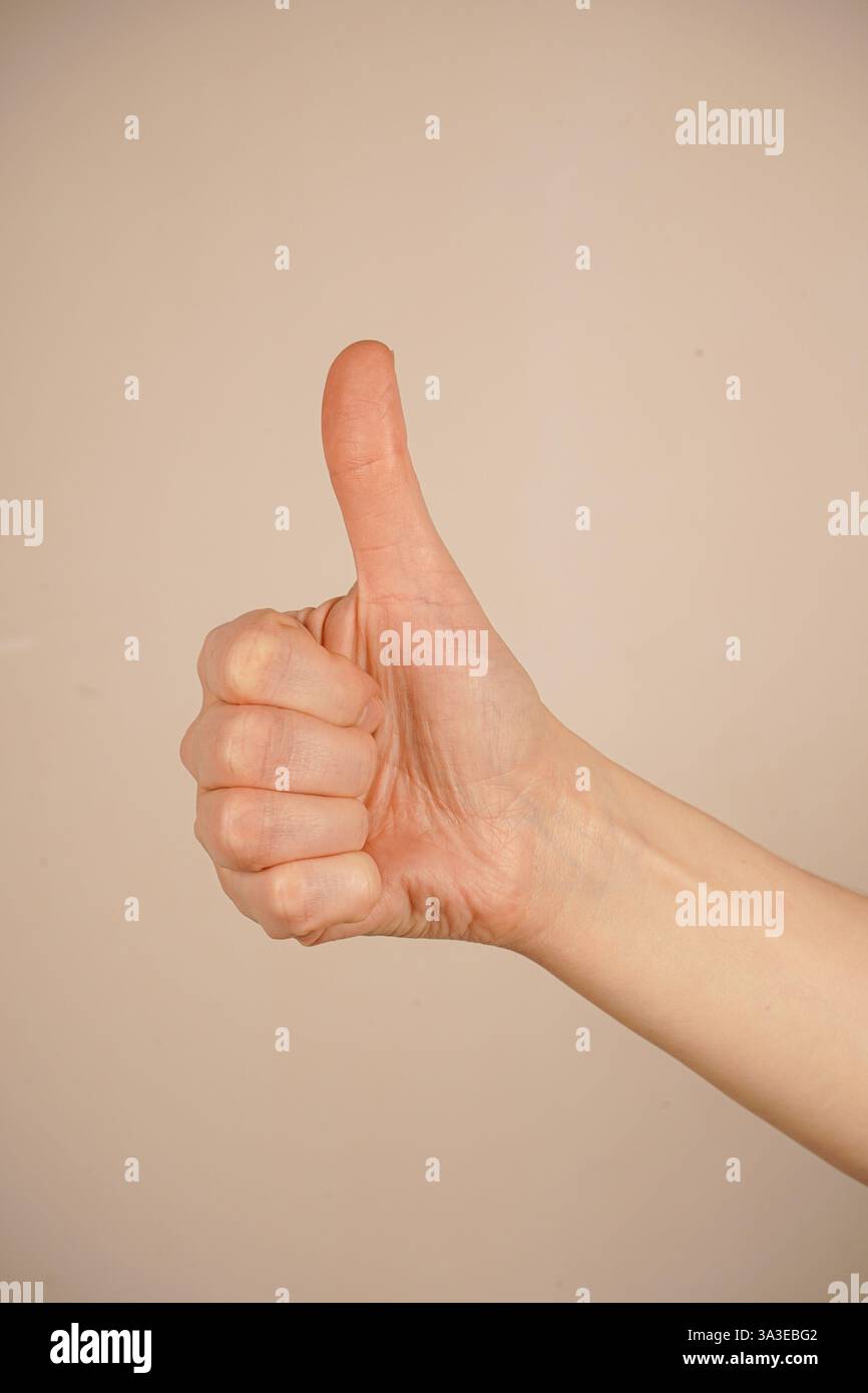 A hand giving a thumbs-up sign against a neutral, bright wall. The ...