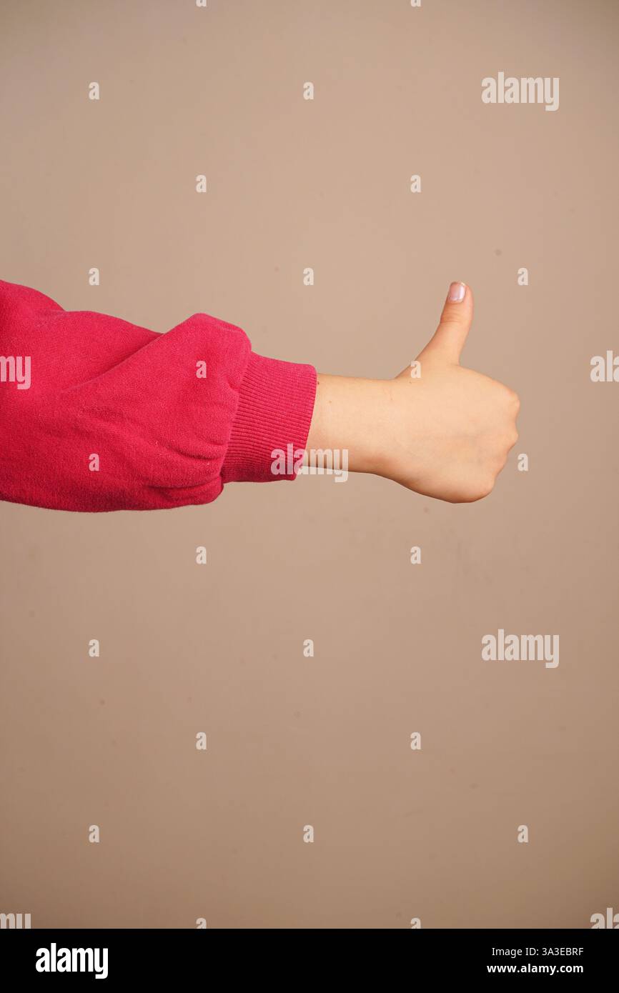 A hand giving a thumbs-up sign against a neutral, bright wall. The ...