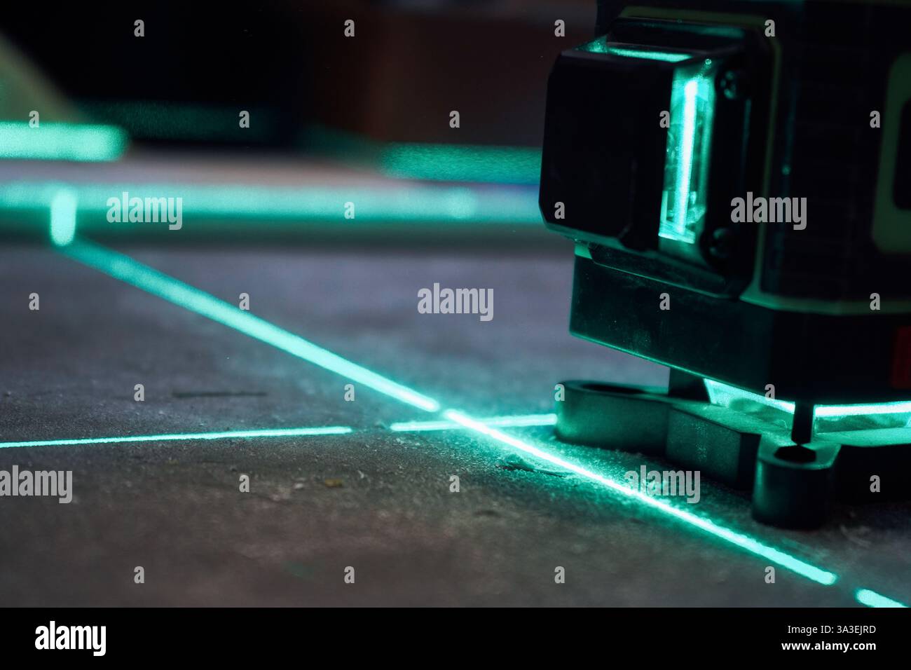 In an unfinished room, two green laser lines overlap on the floor ...