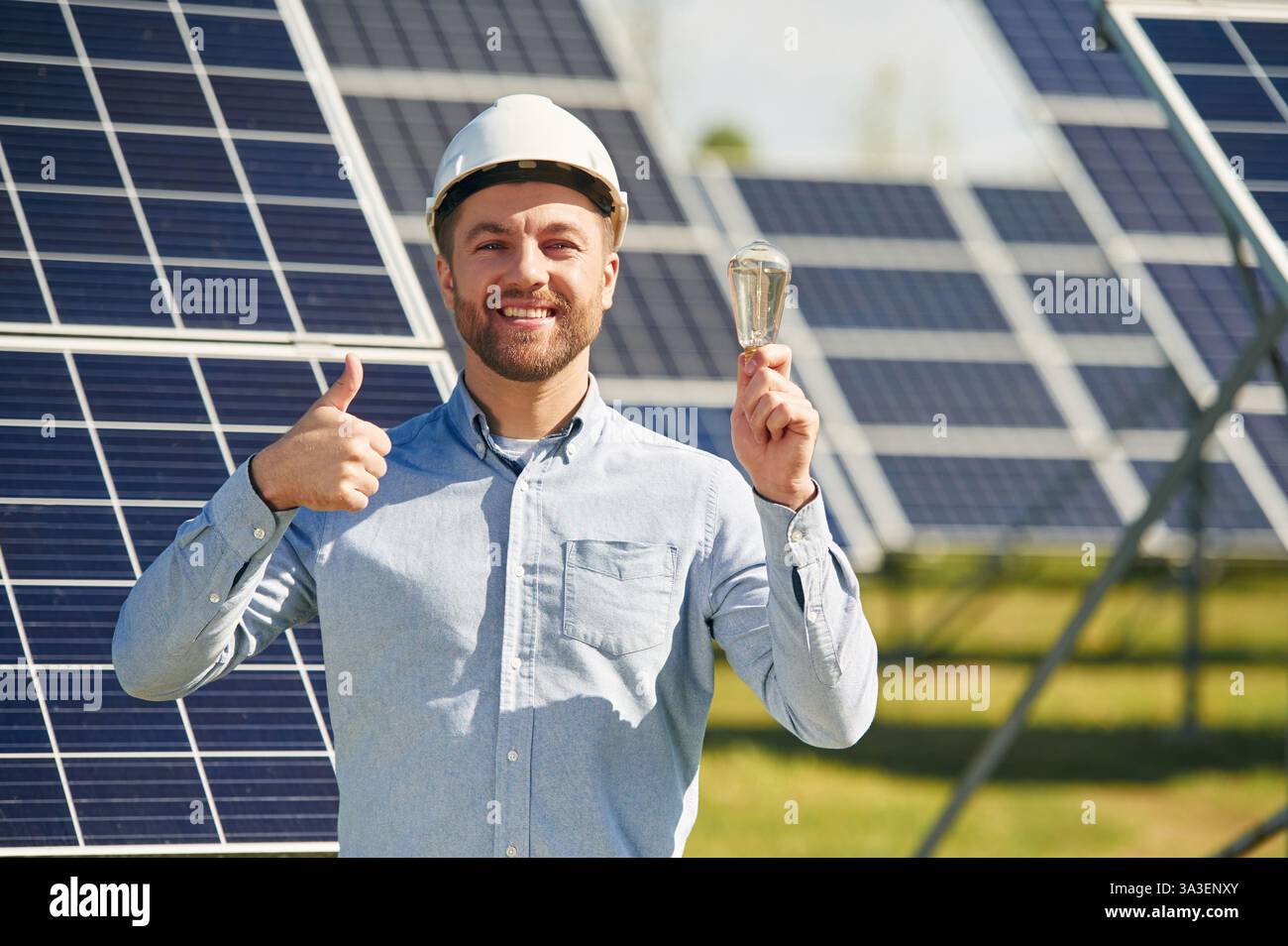 Smiling and holding bulb. Engineer with photovoltaic solar panels ...
