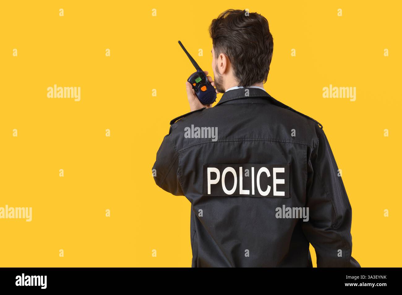Male police officer with radio transmitter on yellow background, back ...