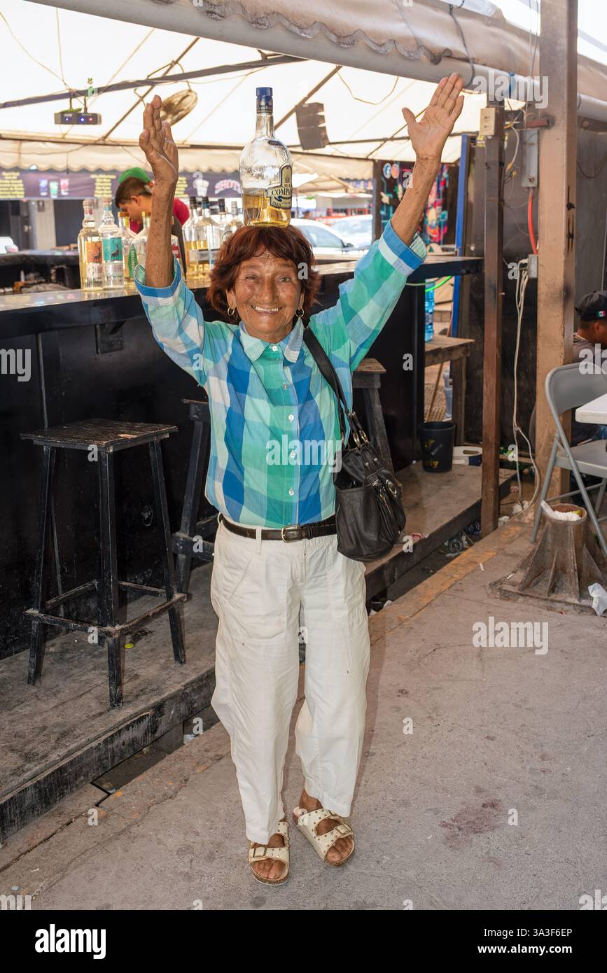 Senior woman dances in front of outdoor bar with liquor bottle on her ...