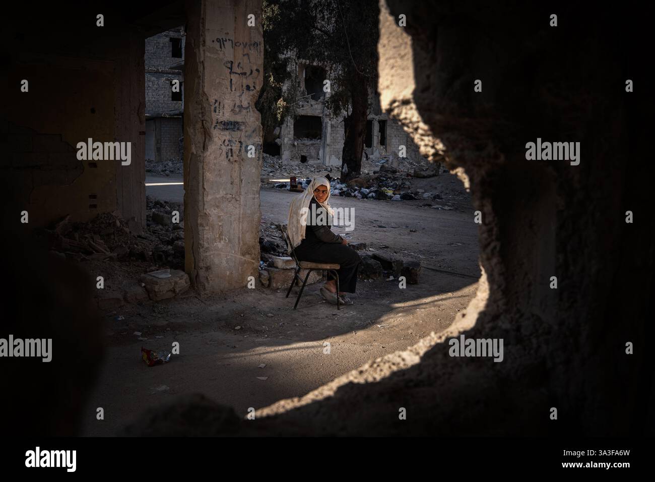 A Syrian-Palestinian refugee sits next to a building razed by the ...