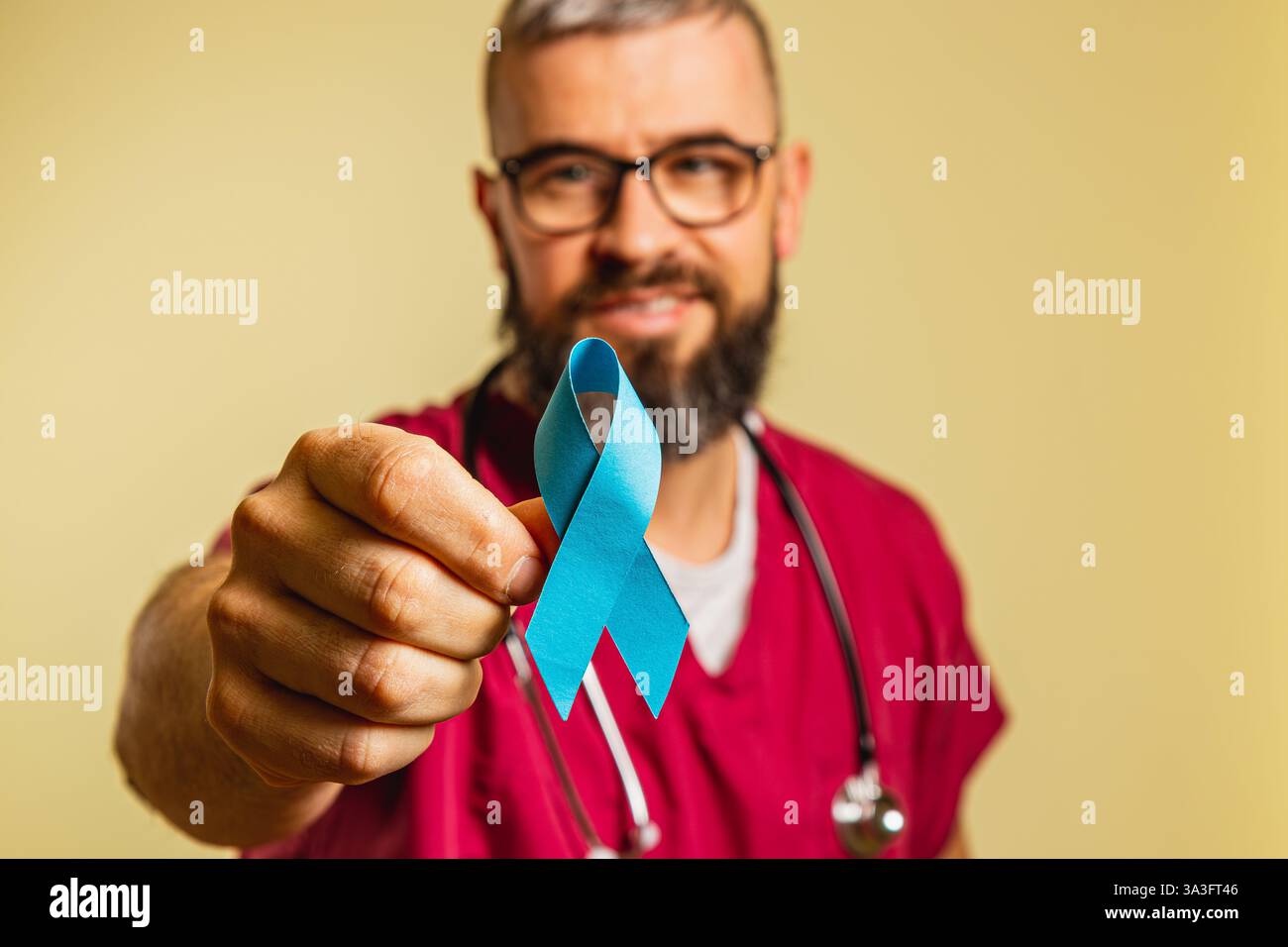 A young male cardiologist wearing scrubs and a stethoscope proudly displays a blue awareness ...