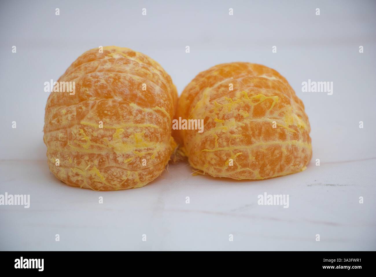 Two mandarins, whole and without skin, with orange rind, lying on a ...