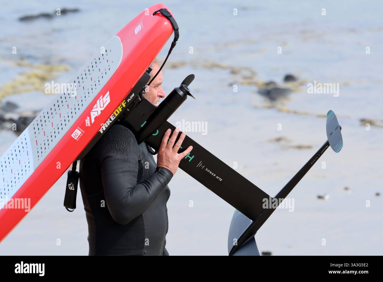 Surfer carrying motorized hydrofoil surfboard at the beach, showing ...