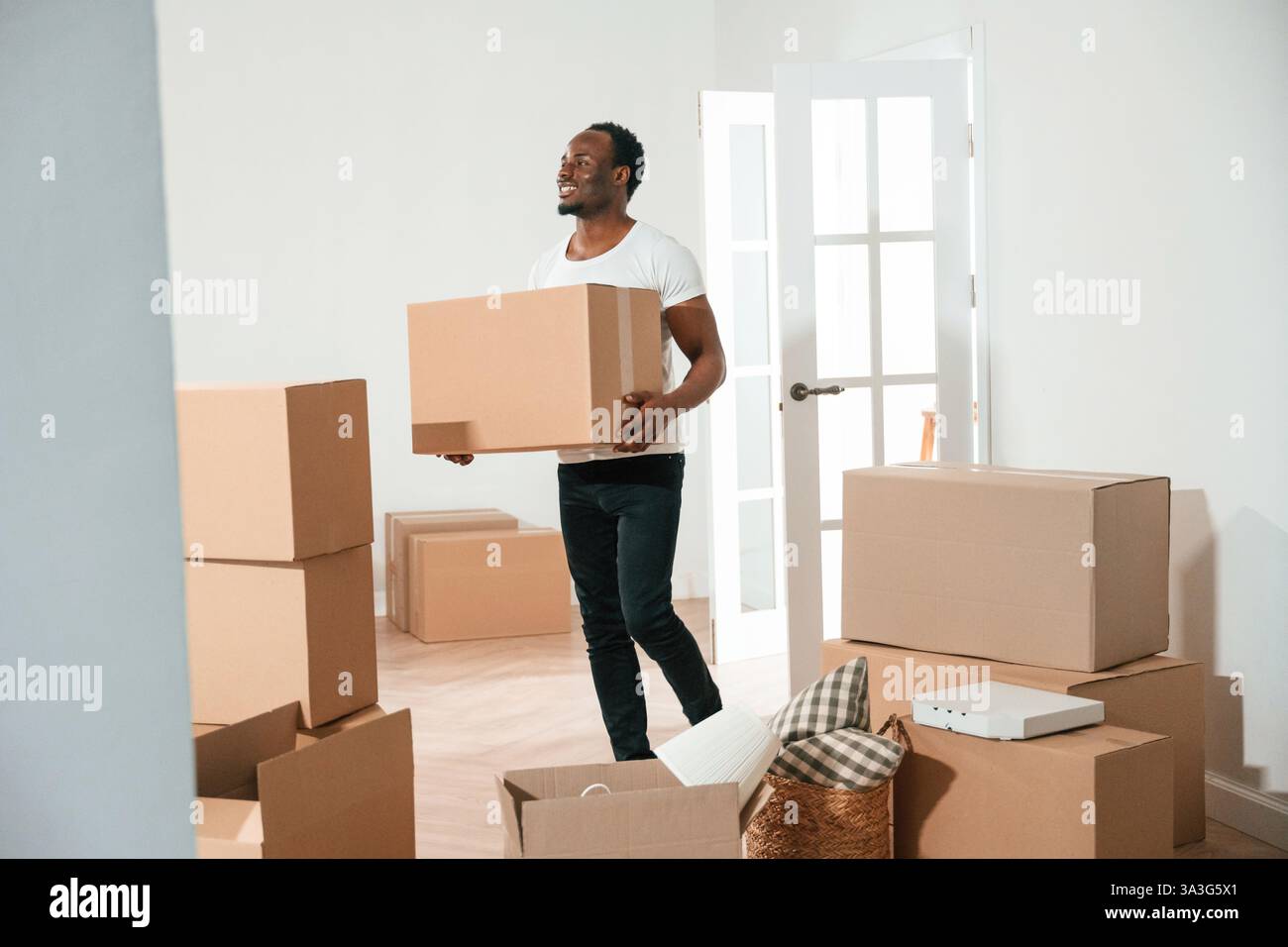 Happy black man is moving in his new home, holding box Stock Photo - Alamy